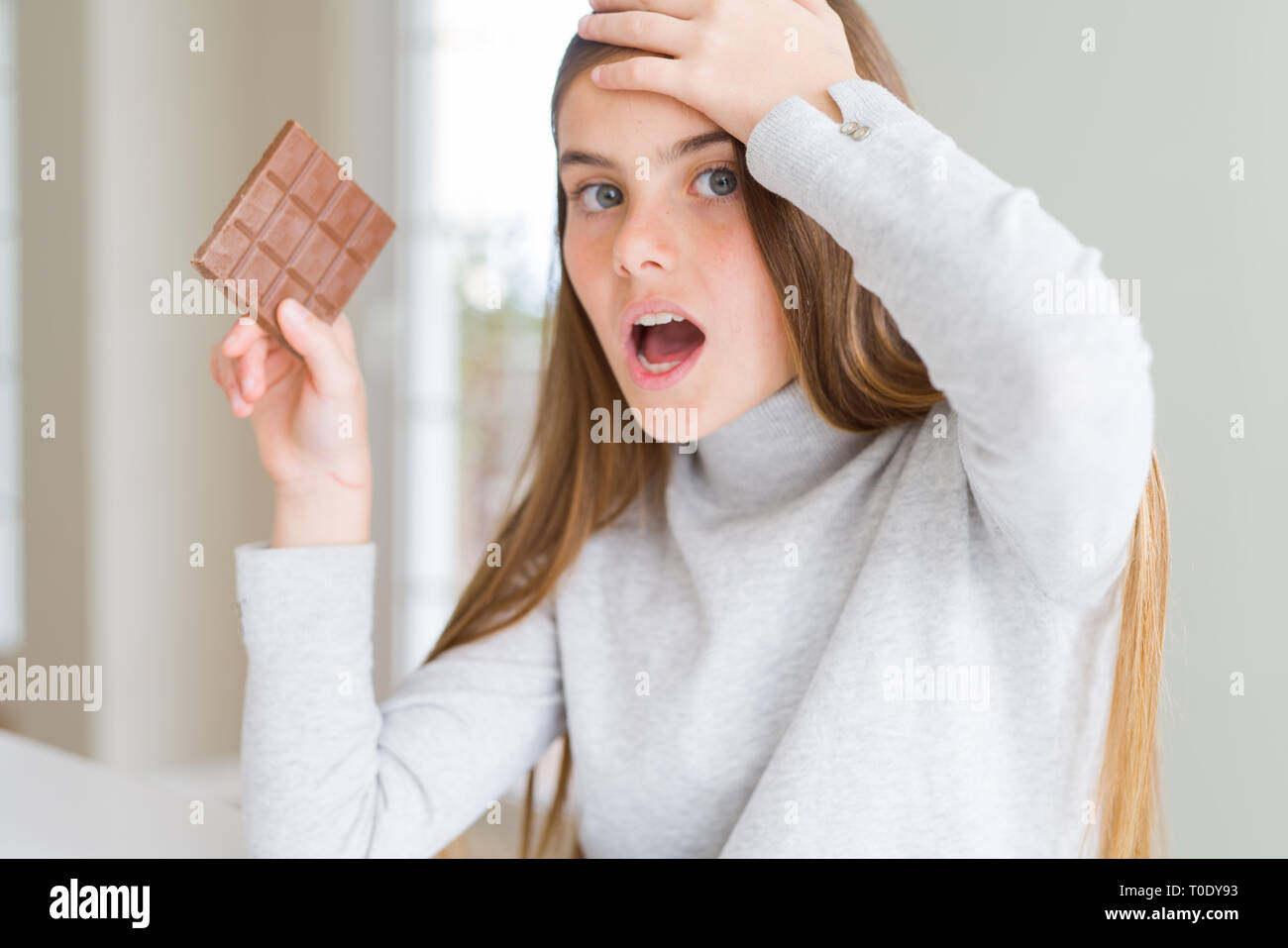 Beautiful young girl kid eating chocolate bar stressed with hand on ...