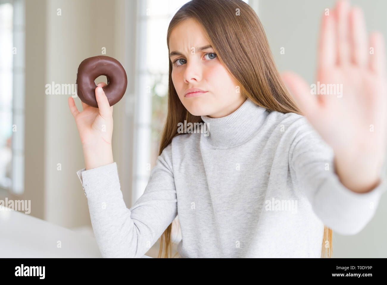 Beautiful young girl wearing eating a chocolate donut with open hand ...
