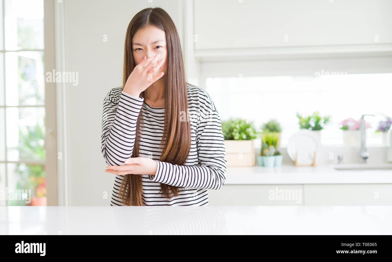 Beautiful Asian woman wearing stripes sweater smelling something stinky ...