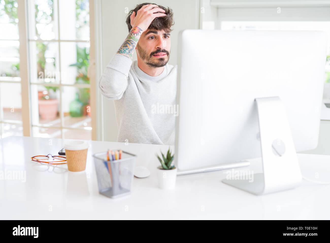 Young man working using computer stressed with hand on head, shocked ...