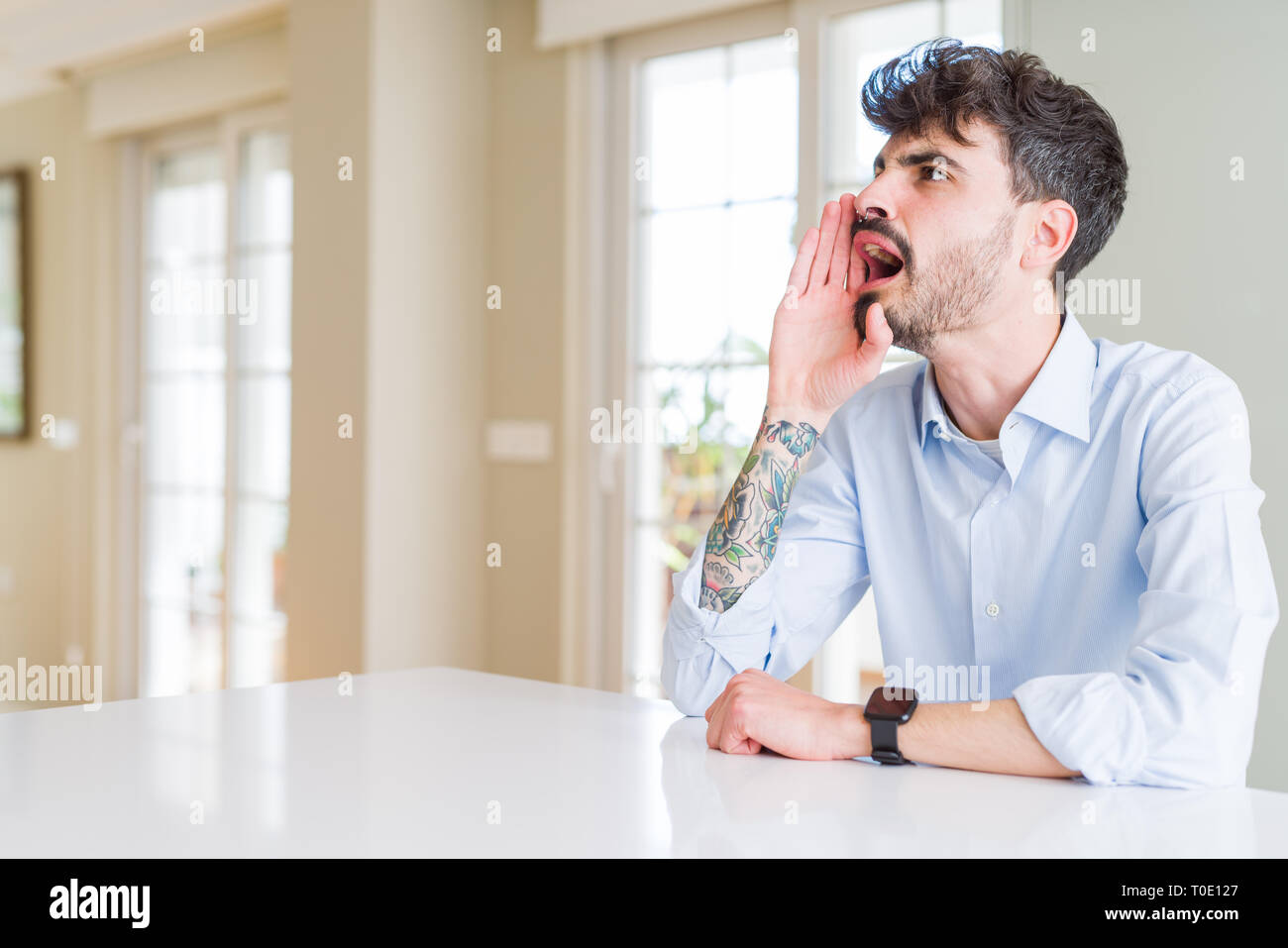 Young businesss man sitting on white table shouting and screaming loud ...