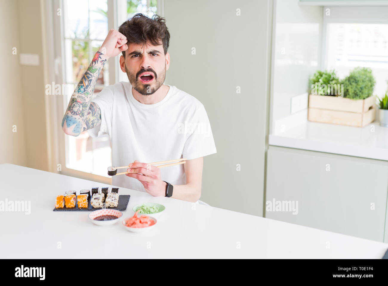 Young man eating asian sushi from home delivery annoyed and frustrated ...