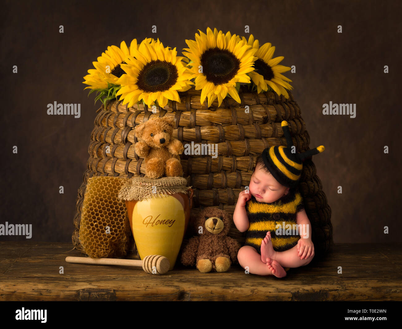 Sleepy cute baby in bee outfit resting against an antique beehive Stock ...