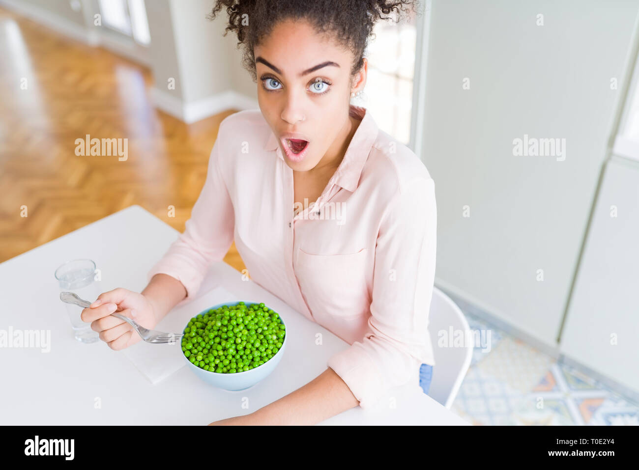 Young african american girl eating healthy green peas scared in shock ...