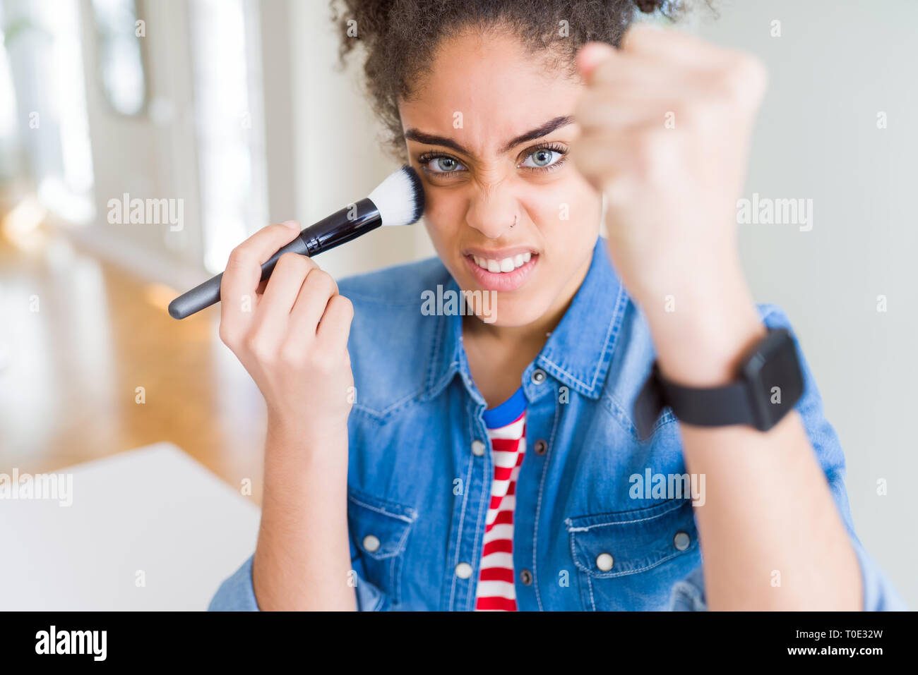 Young african american girl appying blush using make up brush annoyed ...