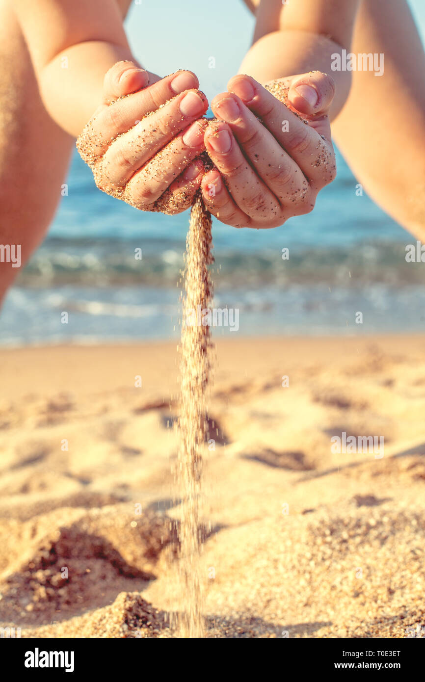 Child playing with sand on sea beach closeup. Sand falling from the ...