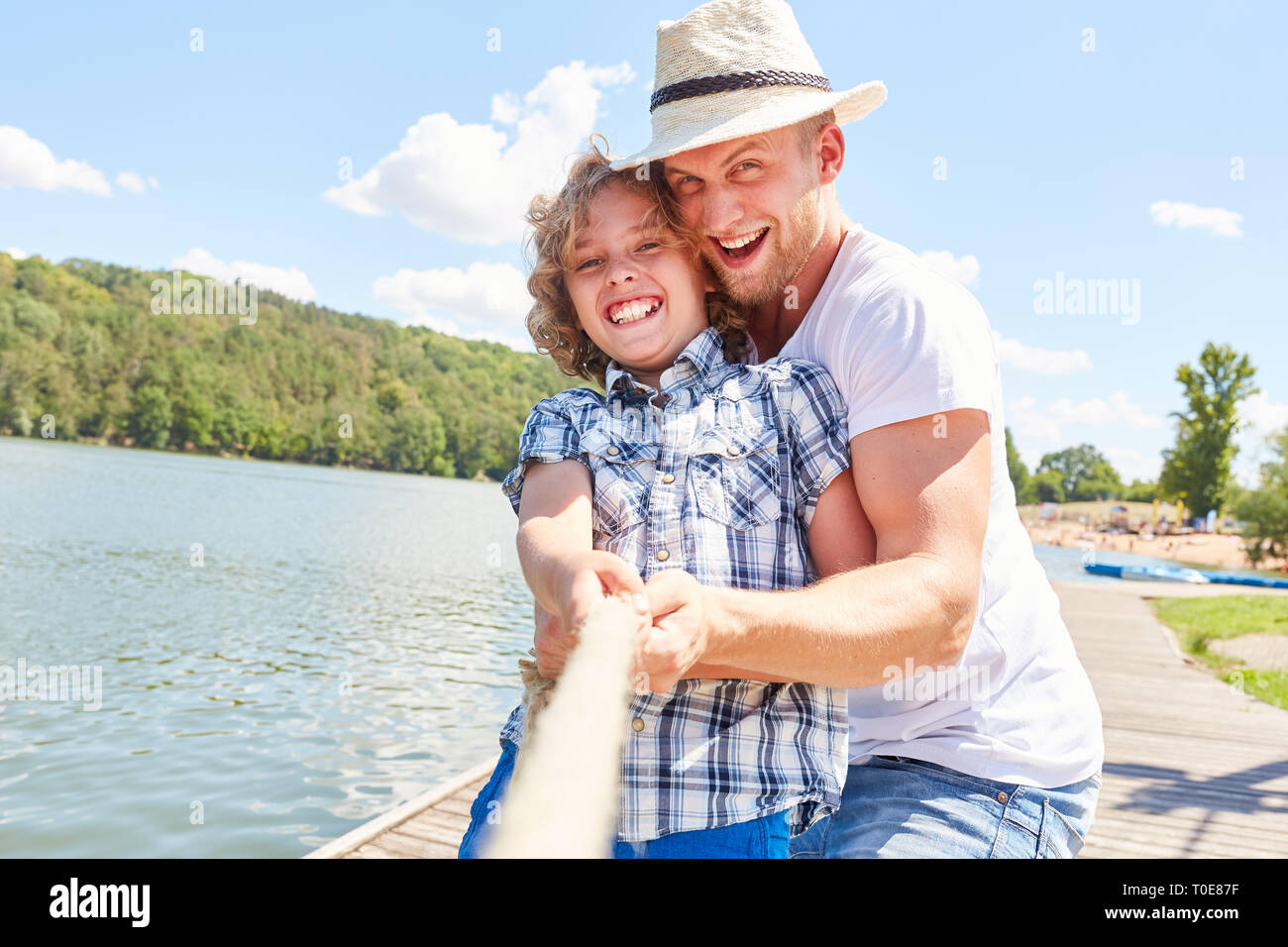 Boy in tug of war with his father at the lake in summer camp or summer ...