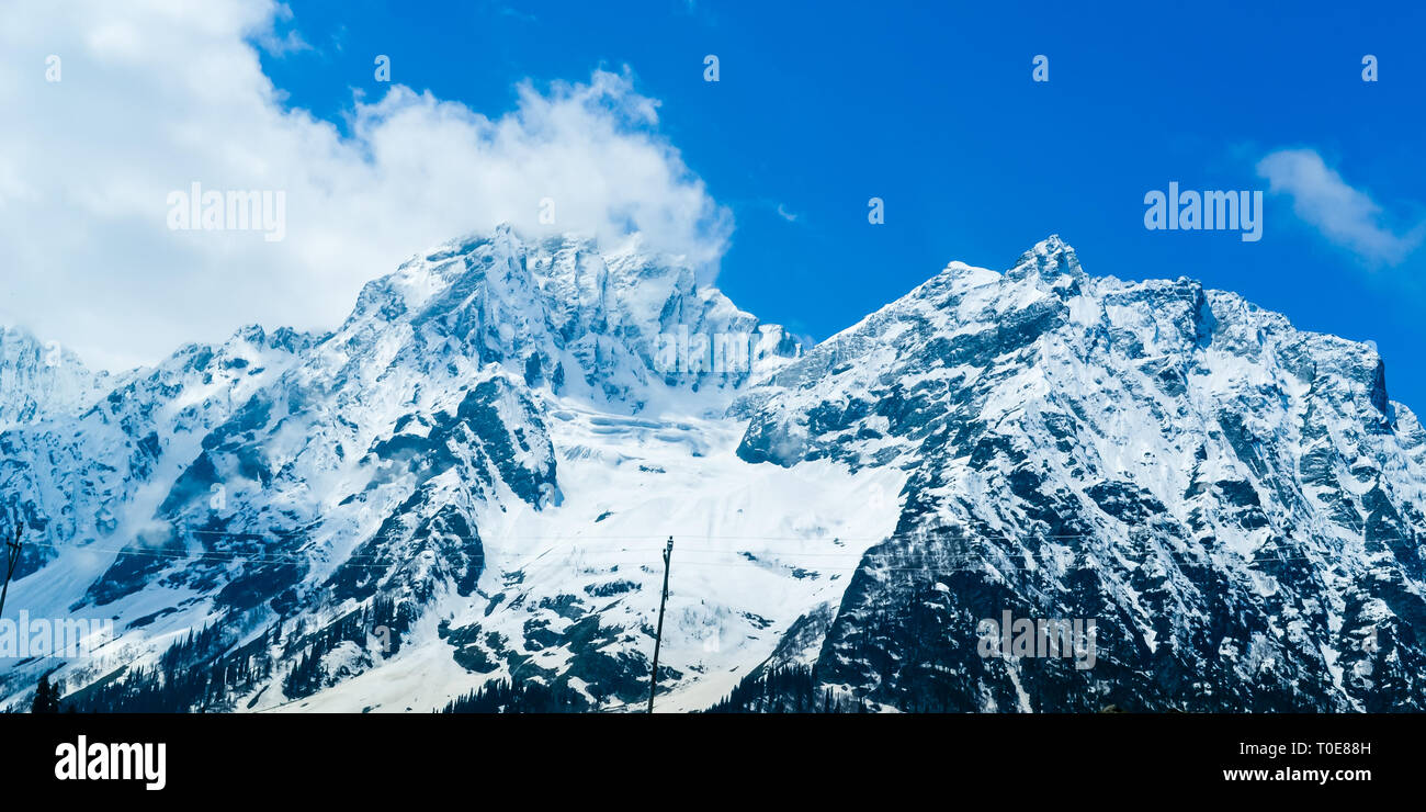 Wide panoramic view of snow covered mountain peak and blue sky with ...