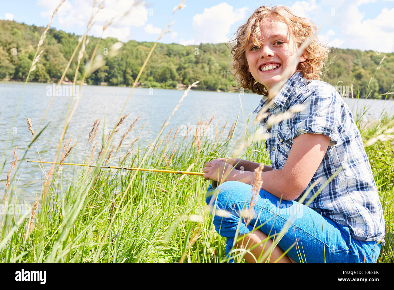 Happy boy in the grass at the lake shore is having fun while fishing in ...