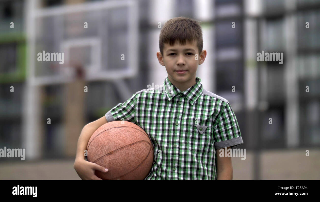 portrait of a boy with a basketball ball on a basketball court, looks ...