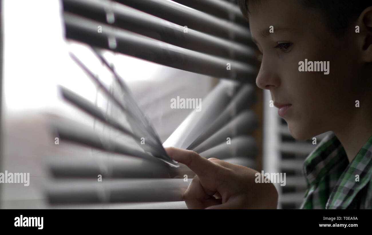 offended boy looks out the window, lowers the blinds, spies, boy is ...