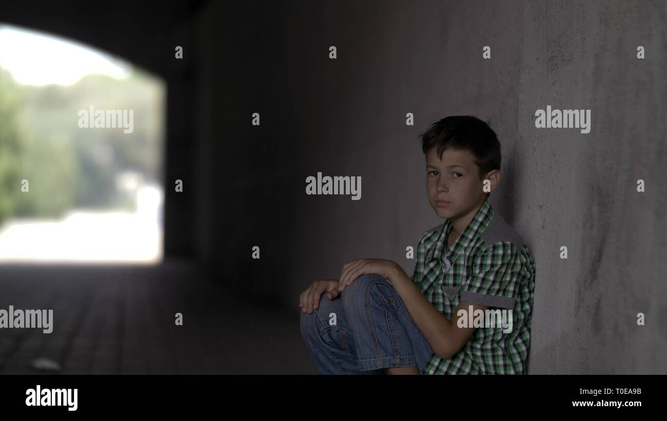 offended abandoned boy sits in a tunnel on the floor, looks at the ...