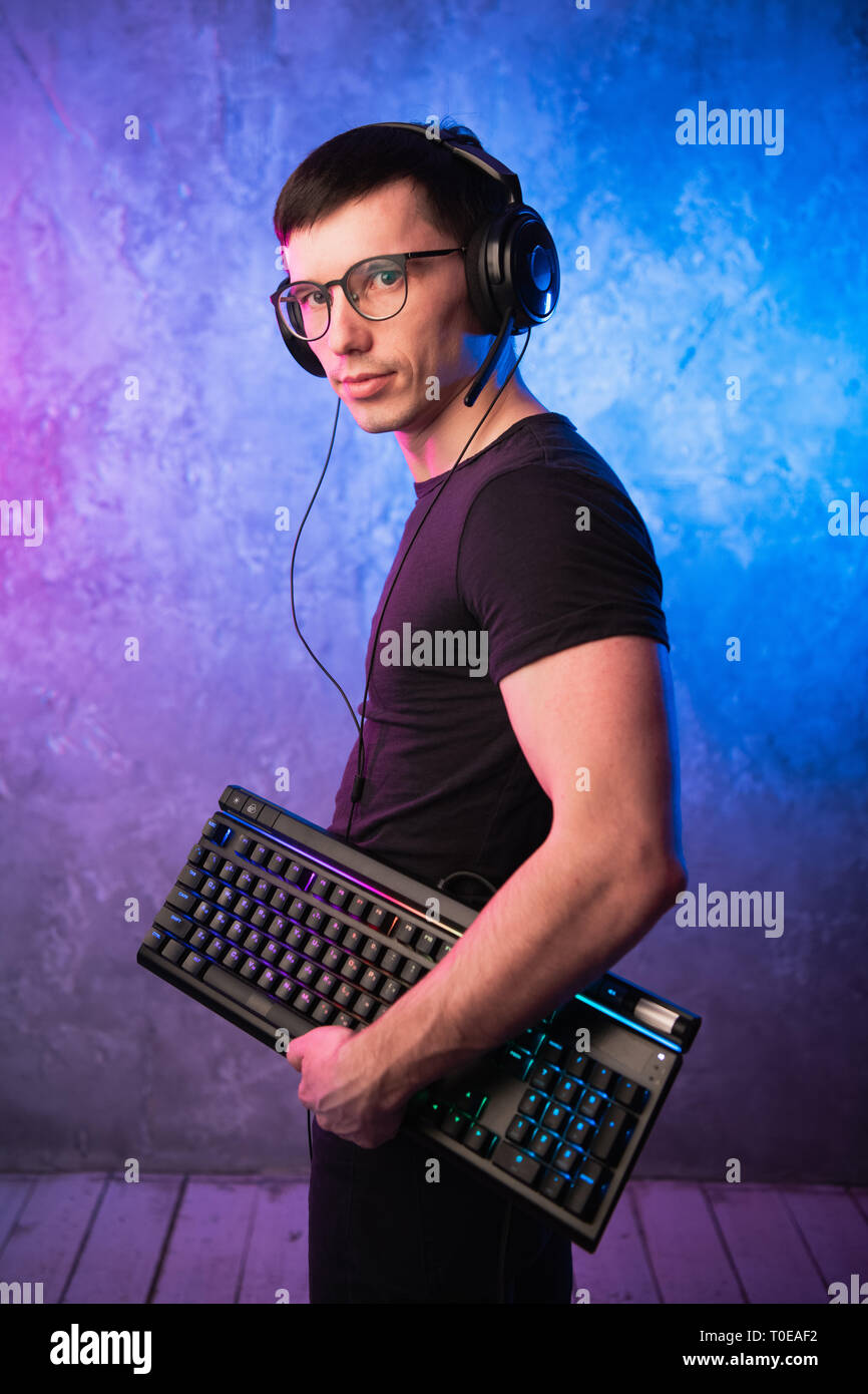 Computer nerd with keyboard over colorful pink and blue neon lit wall ...