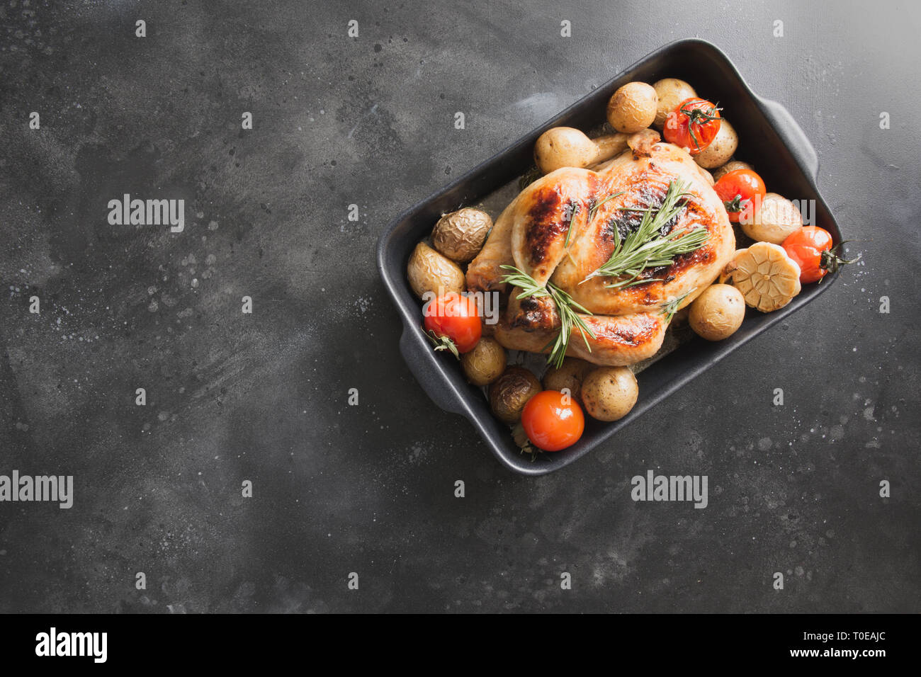 Roasted chicken with potatoes on black table. Dinner. Oven baked food ...