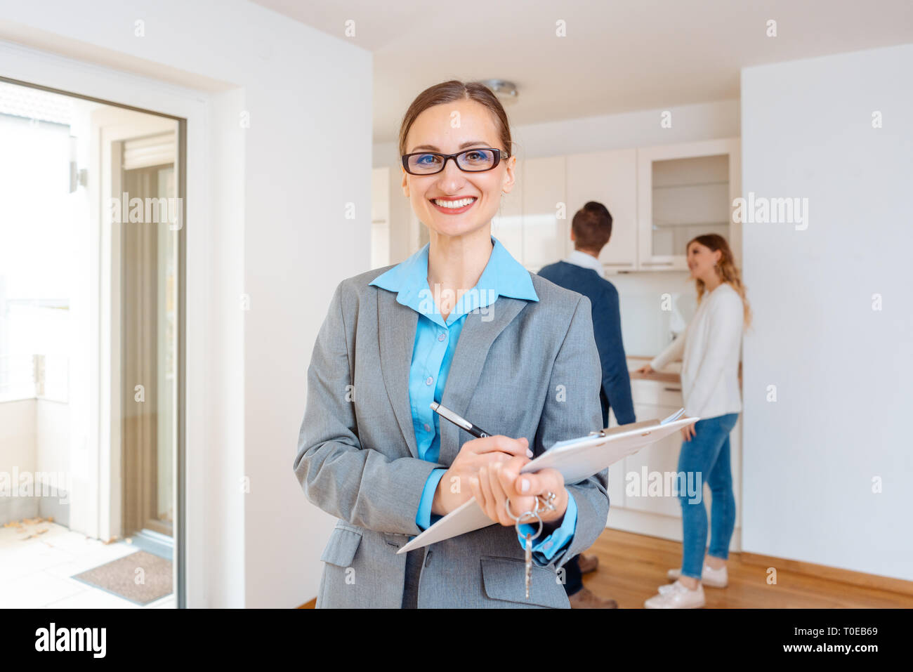 Realtor in new house with couple making the tour in the background ...