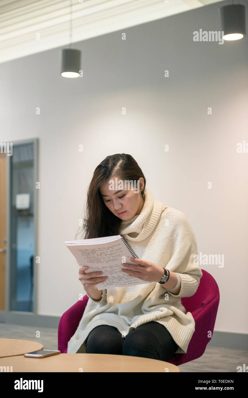 A young asian woman sits and works while reading in the modern communal ...