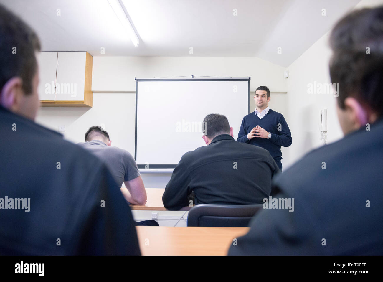 A white man in a blue jumper holds a training presentation for fellow ...