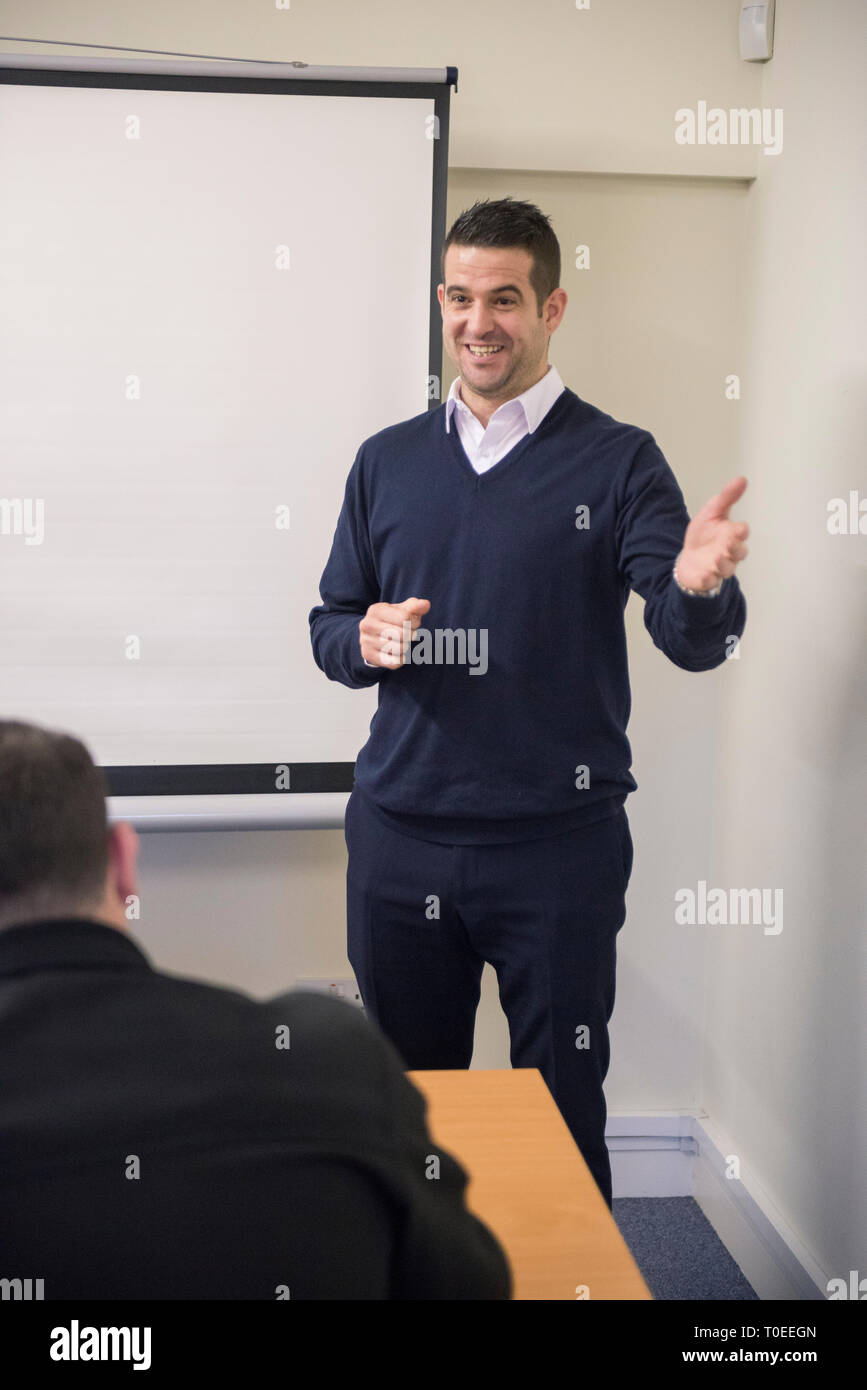 A white man in a blue jumper holds a training presentation for fellow ...