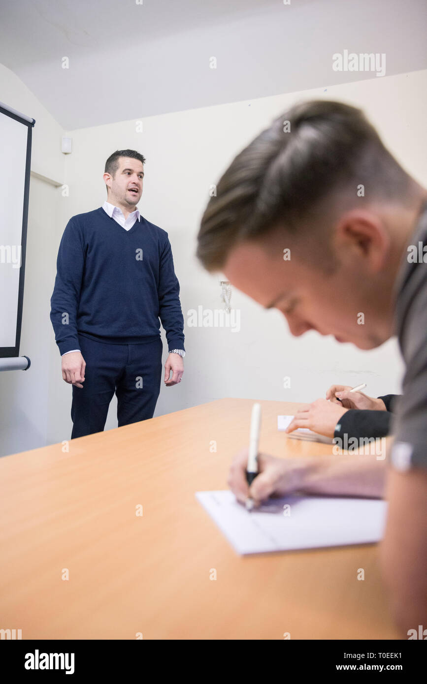 A white man in a blue jumper holds a training presentation for fellow ...