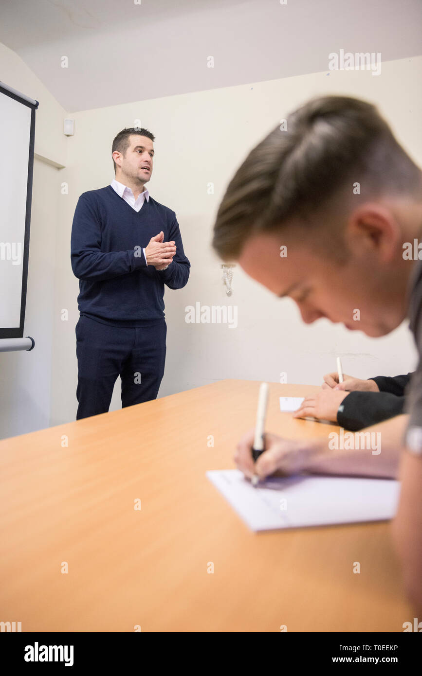 A white man in a blue jumper holds a training presentation for fellow ...