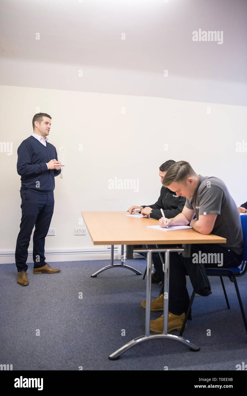 A white man in a blue jumper holds a training presentation for fellow ...