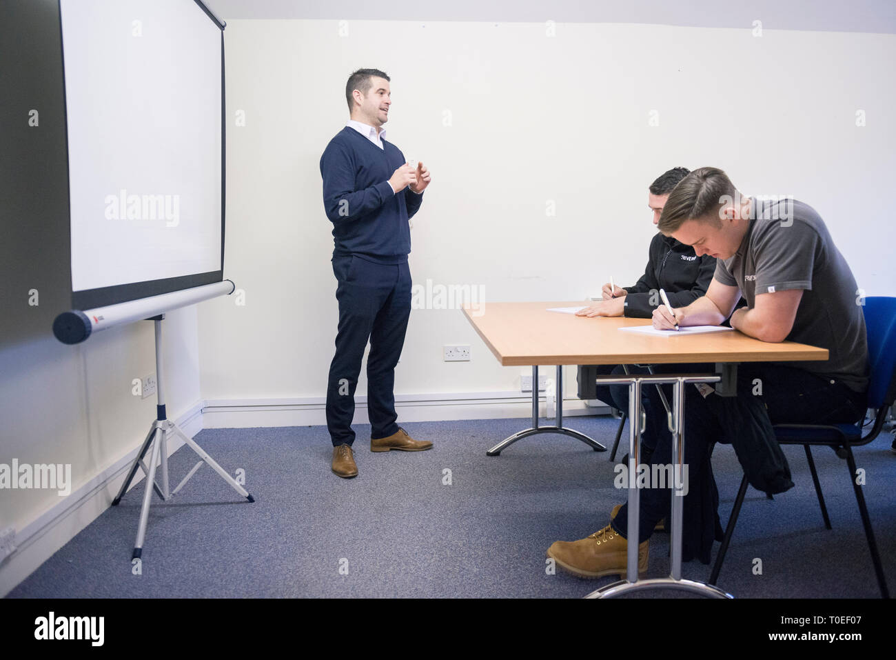 A white man in a blue jumper holds a training presentation for fellow ...