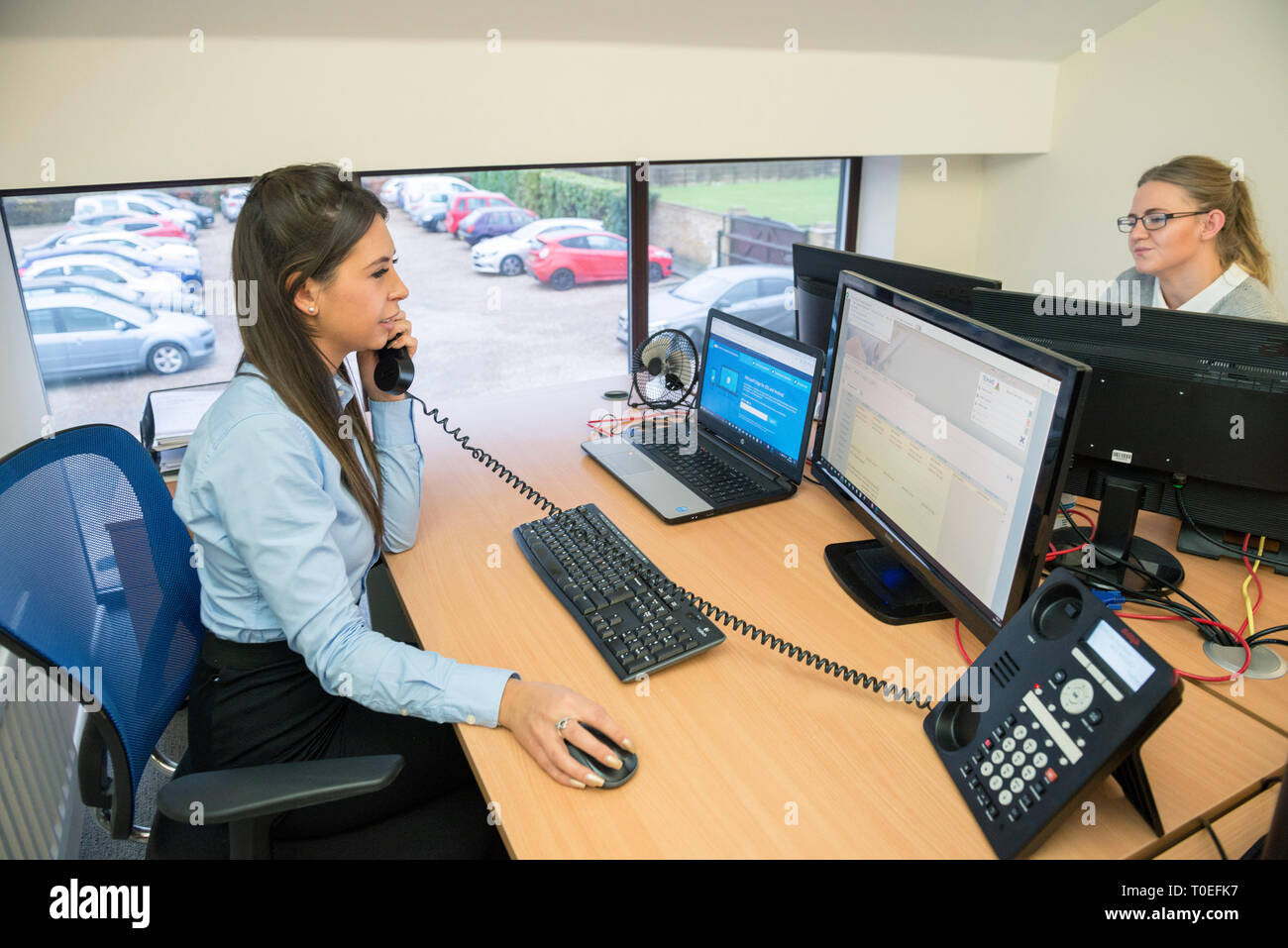 woman on the phone while sat at her desk in an office environment ...
