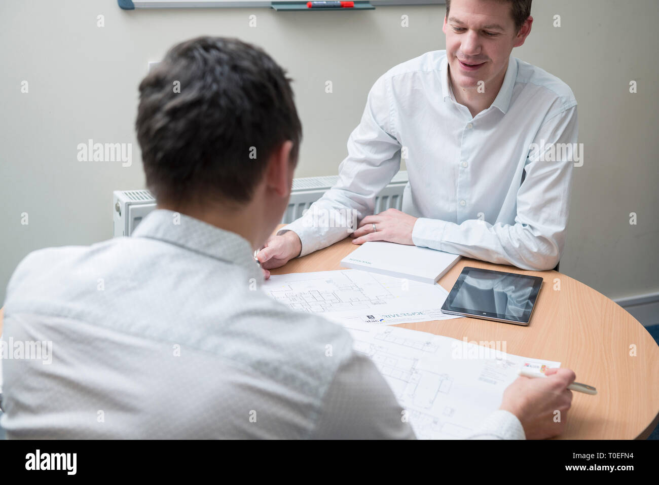 Two men sit round a table in a small office meeting room to review ...
