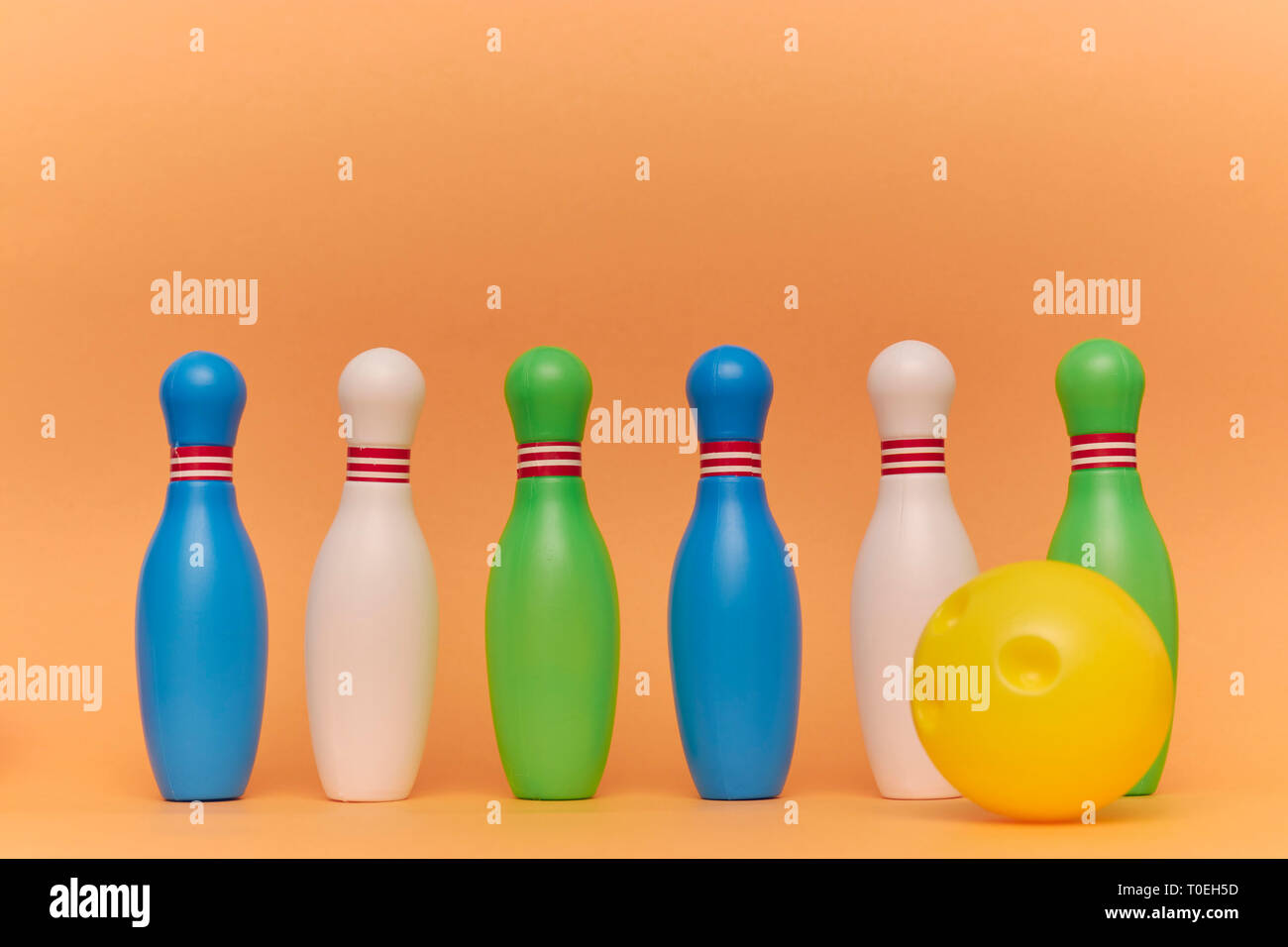 skittles and a ball for playing bowling on a peach background with copy ...