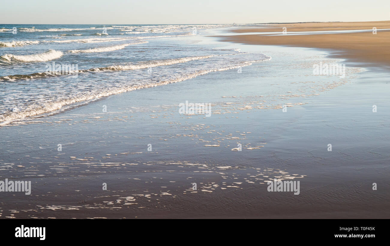 Shoreline with waves lapping the sand on a clear sunny day at Bamburgh ...