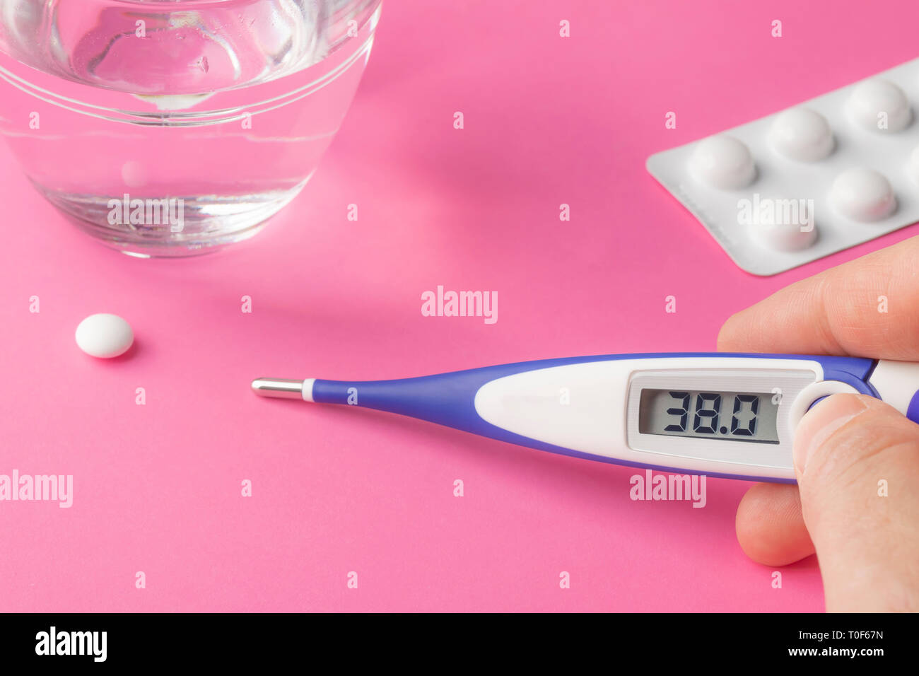 Electronic thermometer and pills on a pink background. High temperature ...