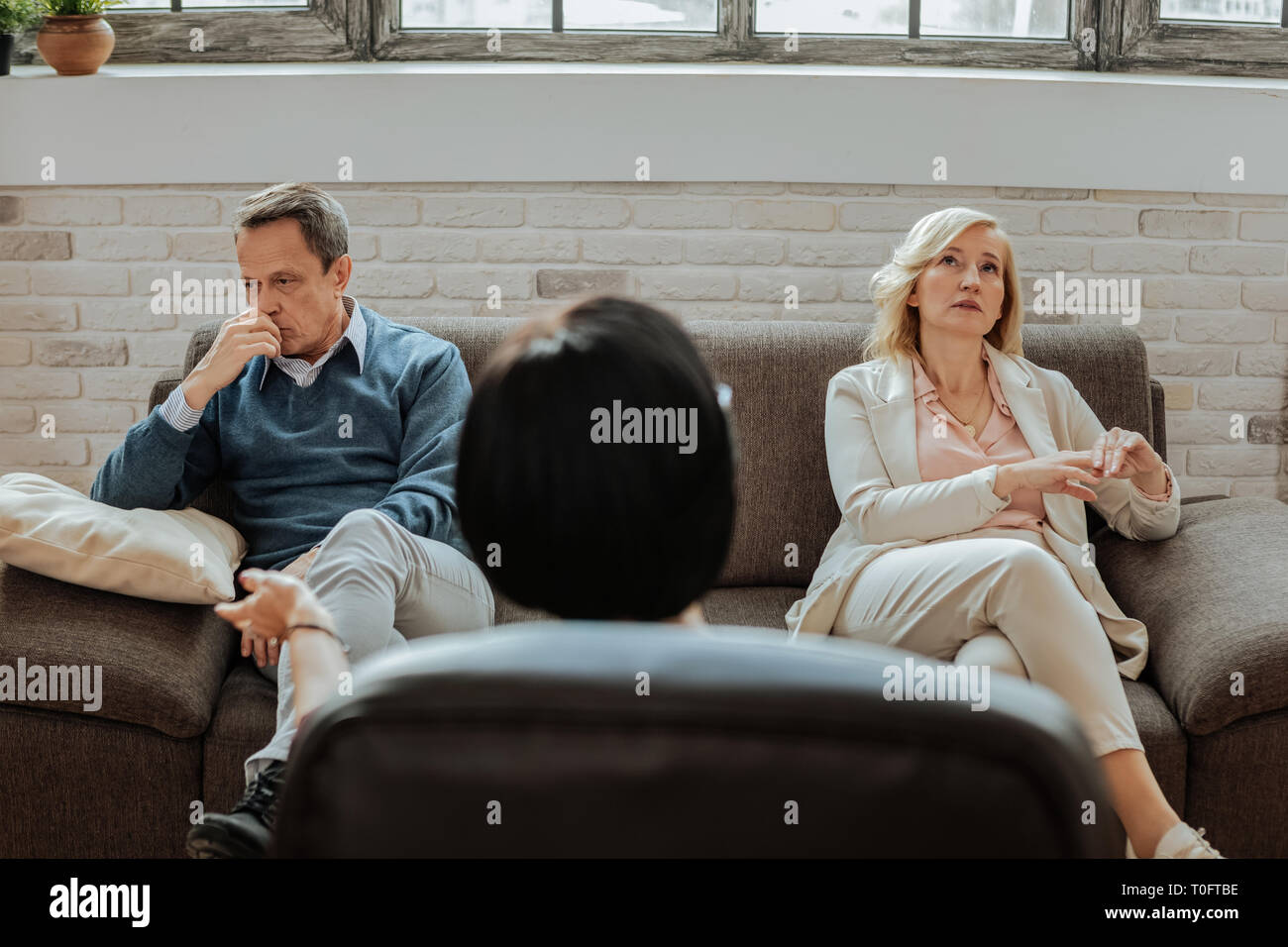 Confused and upset adult couple sitting on different sides of couch ...