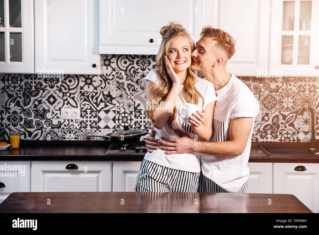 Young blonde man hugs smiling blonde woman during cooking healthy ...