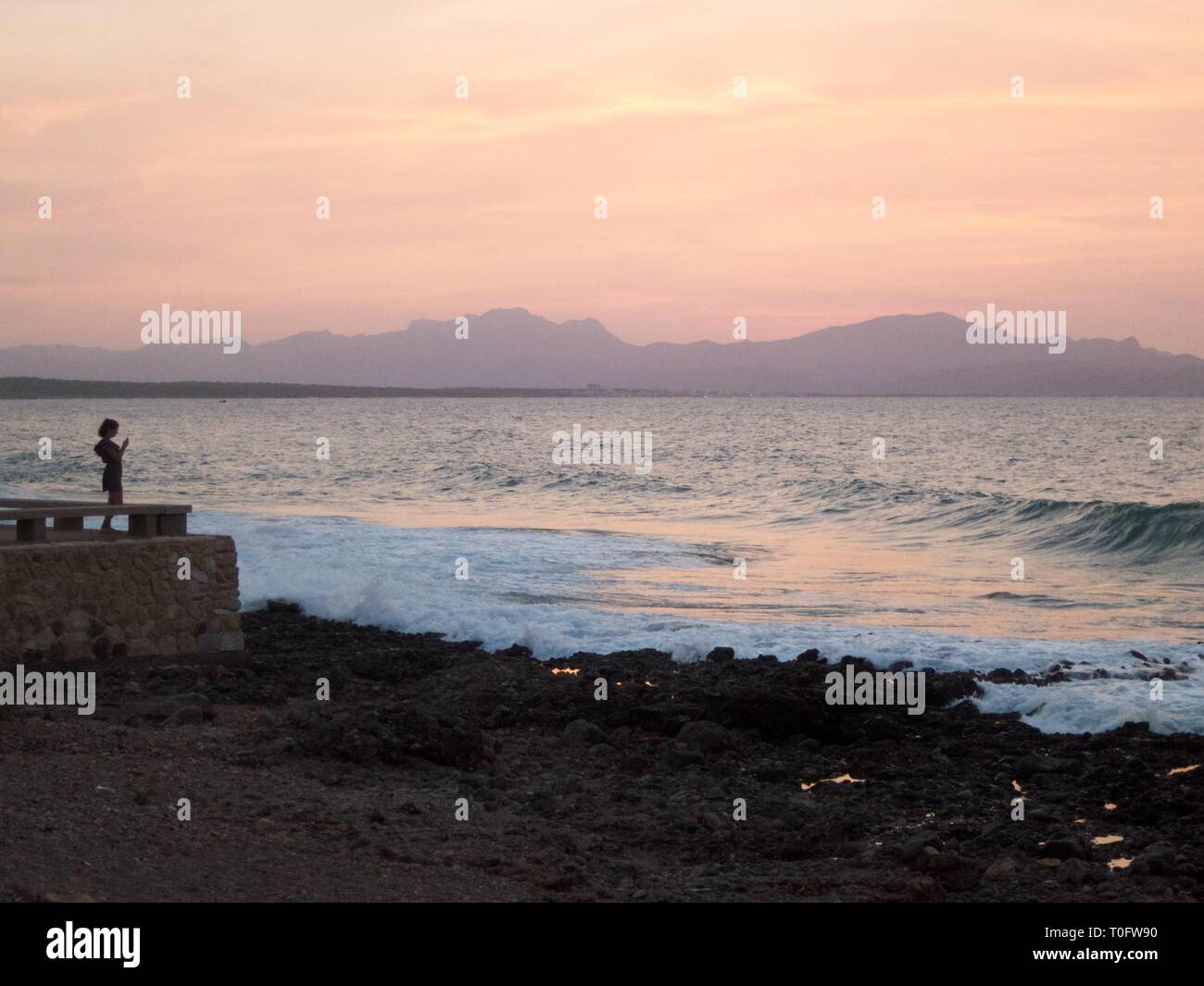 Solitary figure standing on a beach at sunset, Mallorca north coast ...