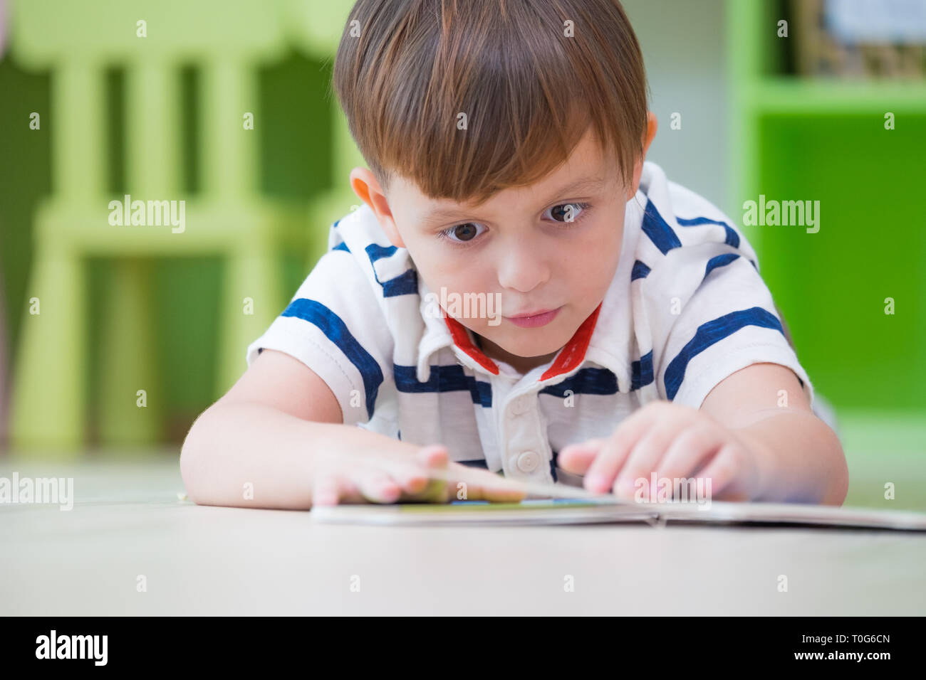 boy kid lay down on floor and reading tale book in preschool library ...