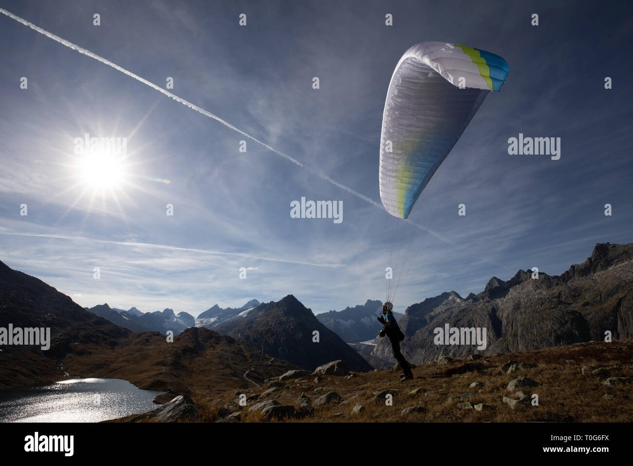 Paraglider Pilot stands on a slope and balances his paraglider above ...