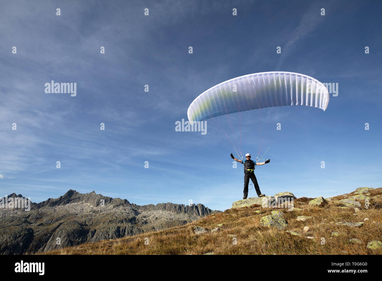 Paraglider pilot stands on a rock and balances his paraglider above his ...