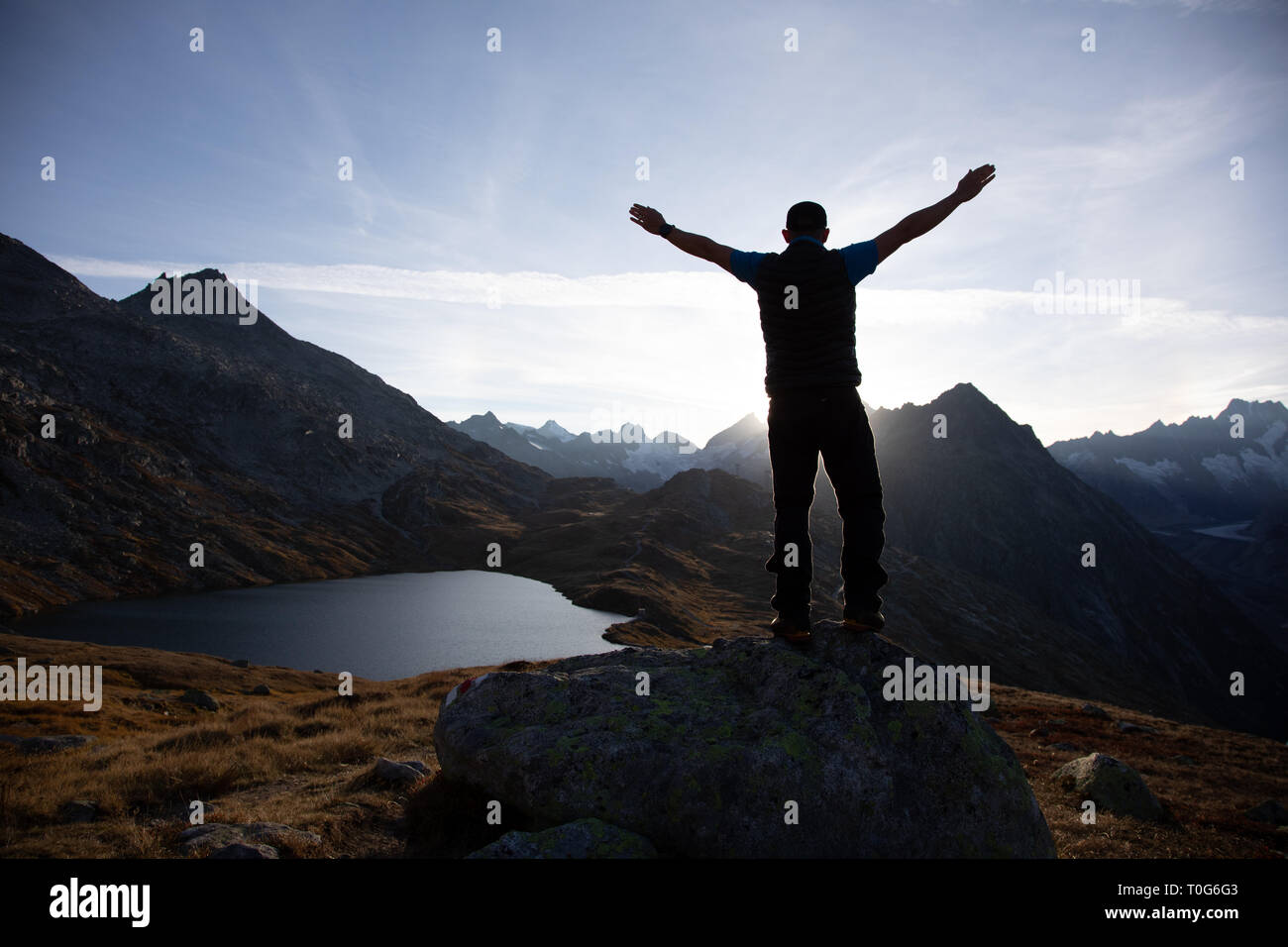 Hiker is standing on a rock with raised hands and enjoying sunrise in ...