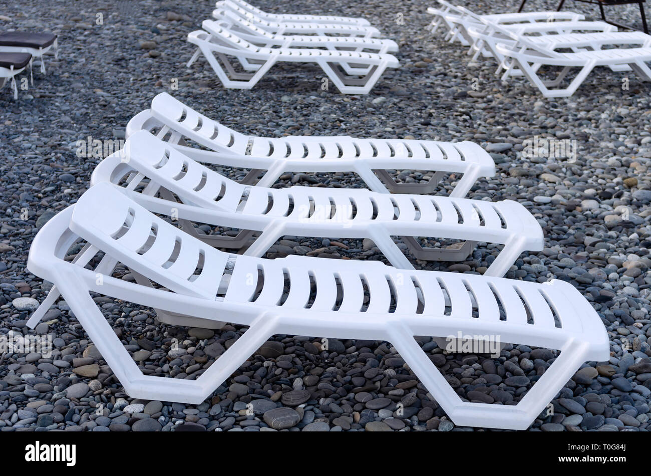 White plastic lounge chairs by the sea. Pebble beach. Free sunbeds on ...