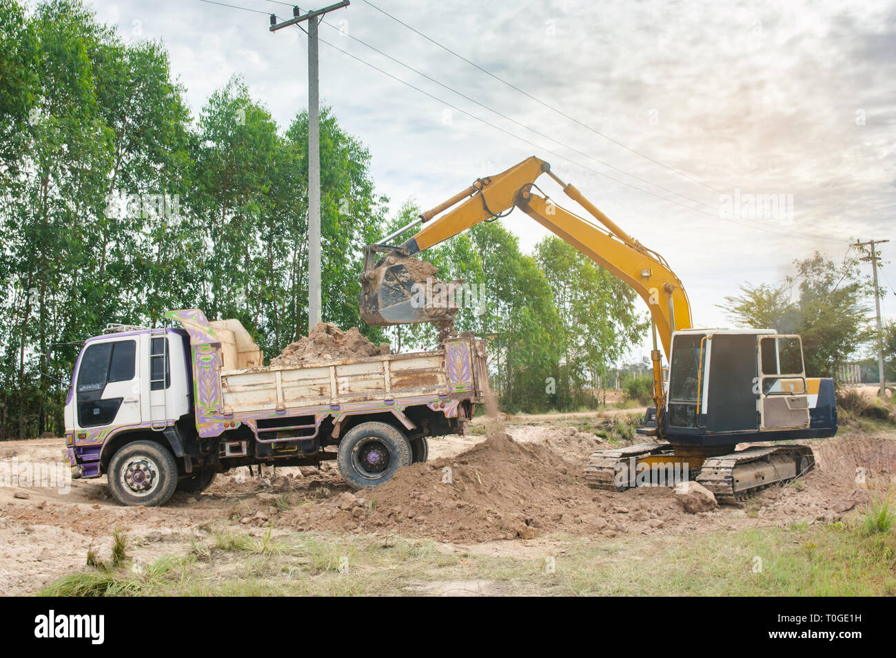 Yellow excavator machine loading soil into a dump truck at construction ...