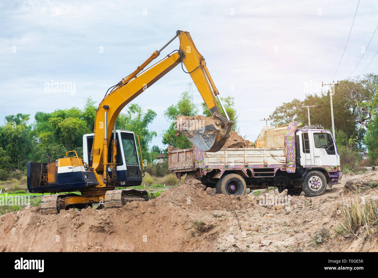 Yellow excavator machine loading soil into a dump truck at construction ...