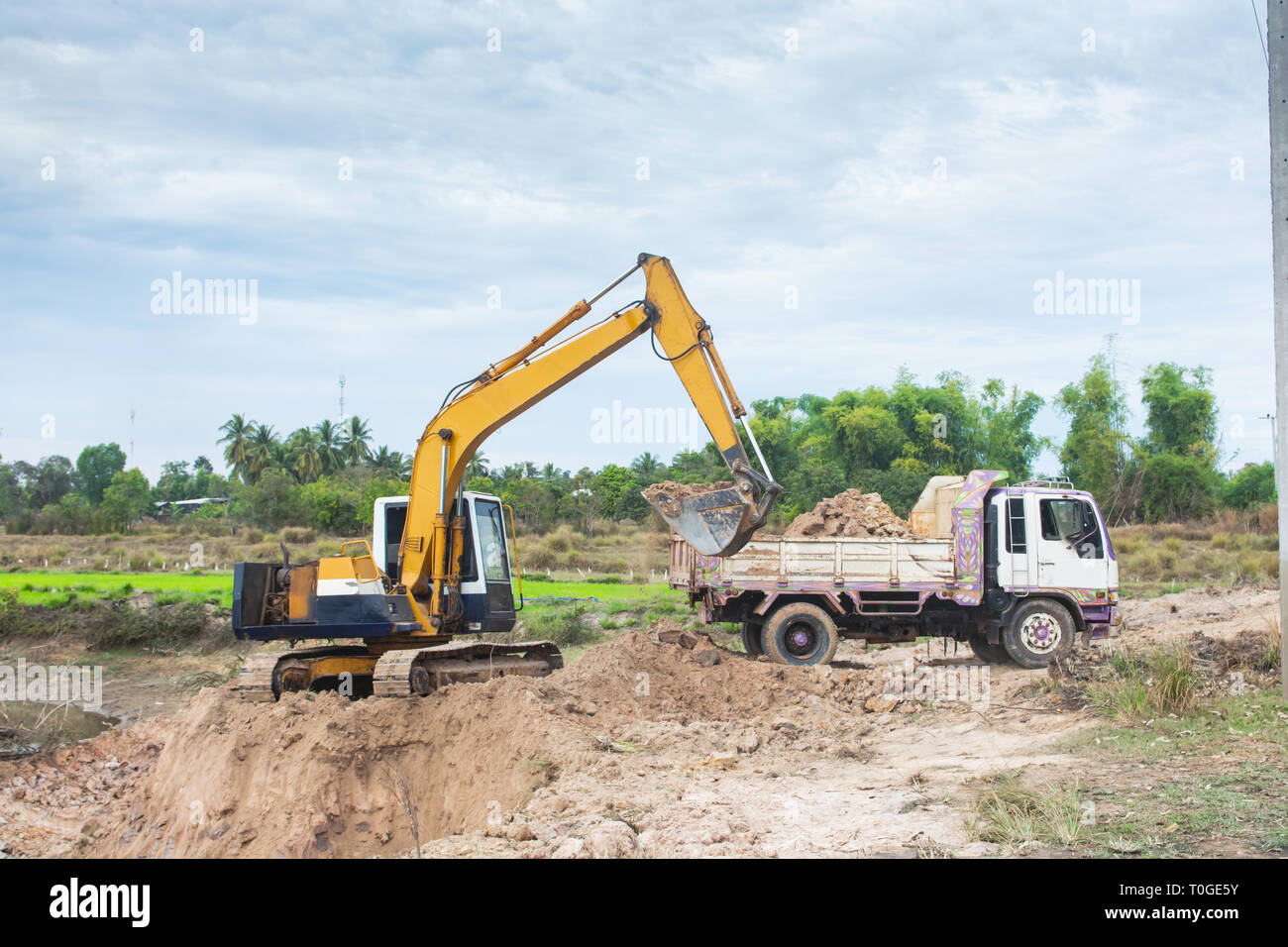 Yellow excavator machine loading soil into a dump truck at construction ...