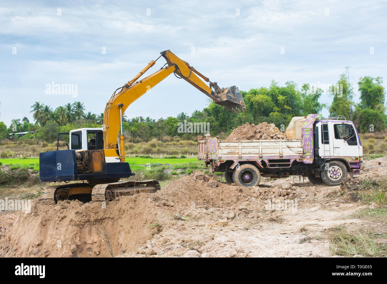 Yellow excavator machine loading soil into a dump truck at construction ...