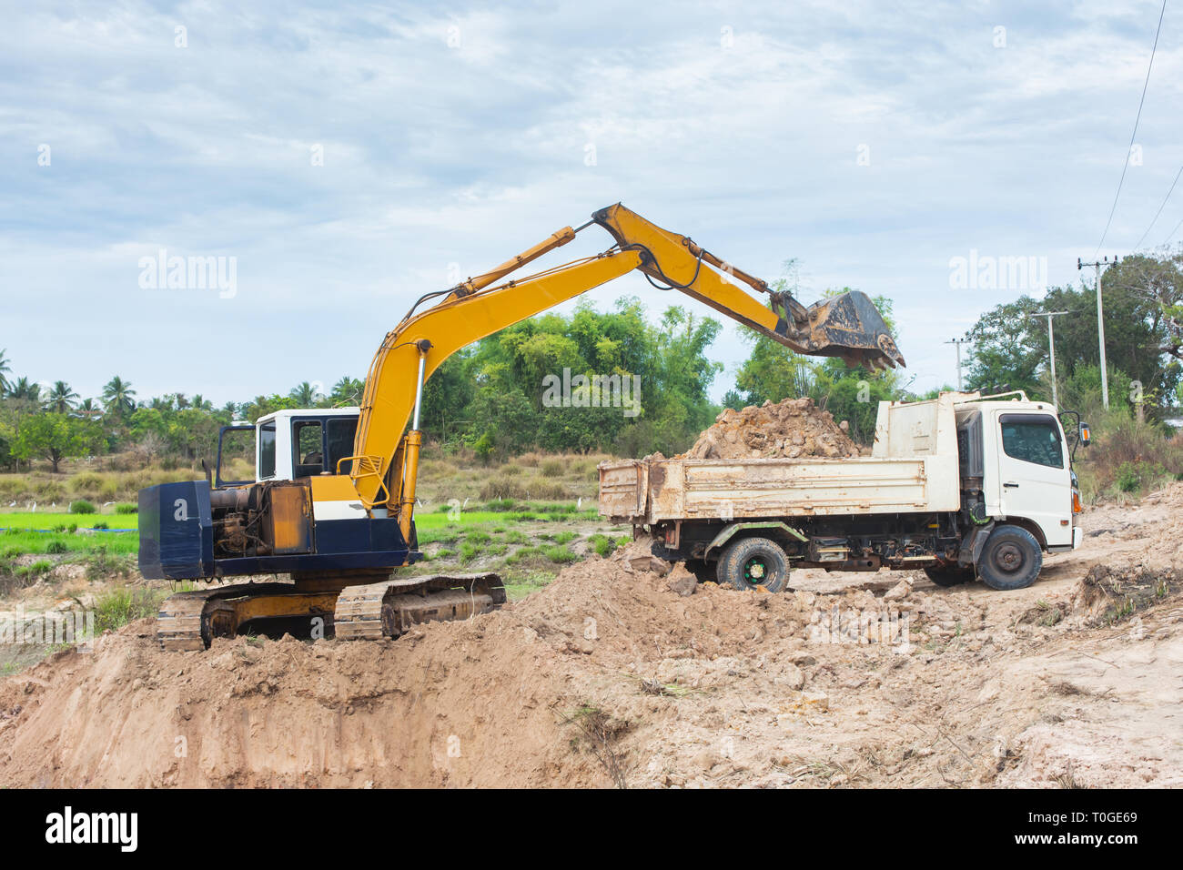 Yellow excavator machine loading soil into a dump truck at construction ...