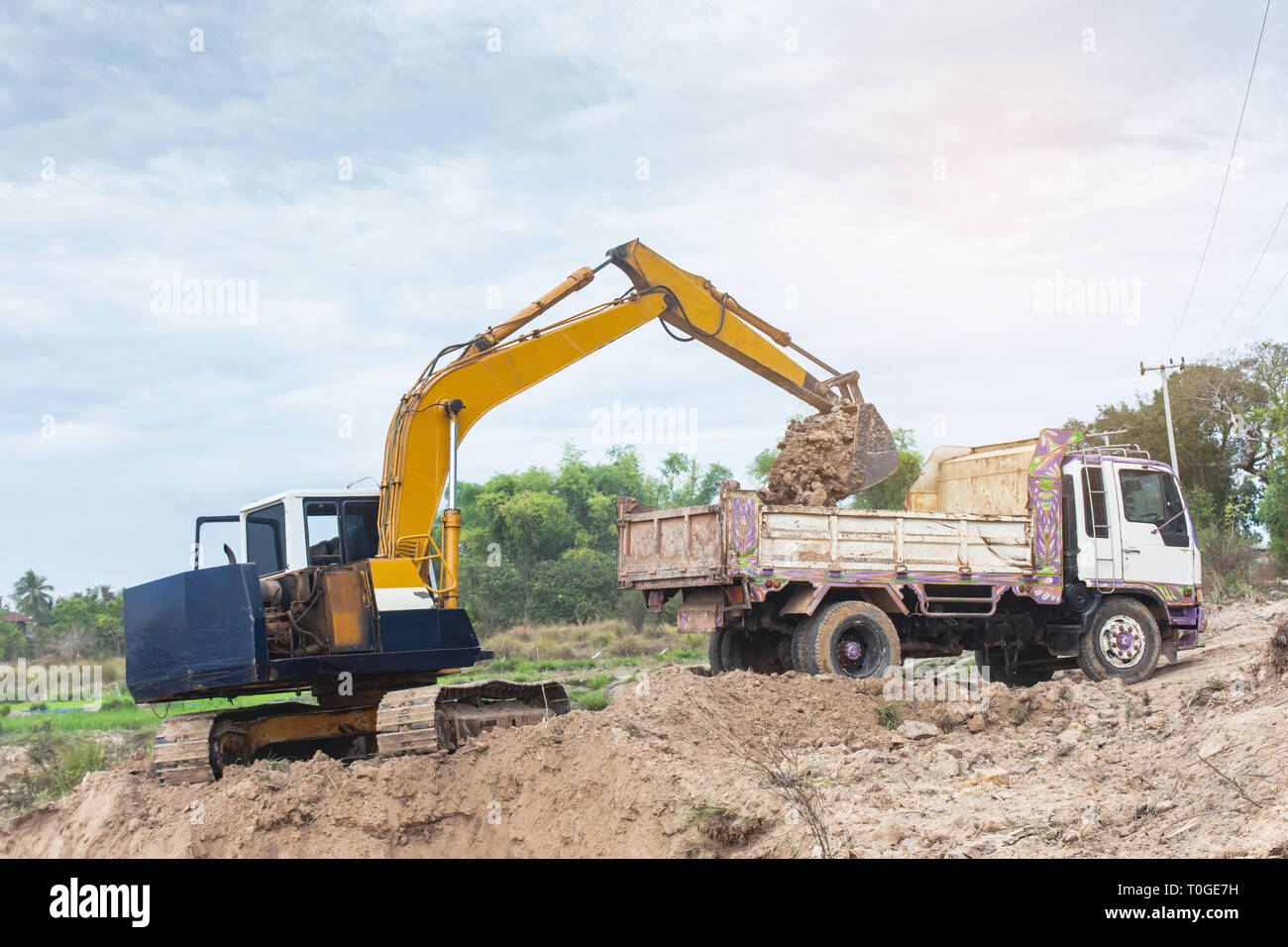 Yellow excavator machine loading soil into a dump truck at construction ...