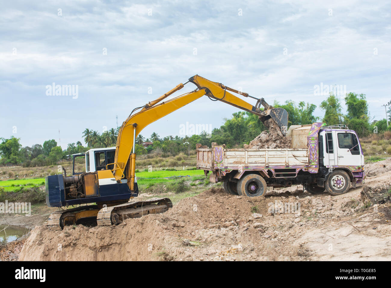 Yellow excavator machine loading soil into a dump truck at construction ...