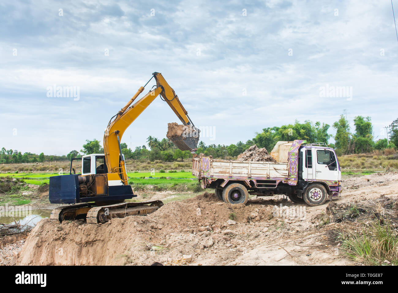 Yellow excavator machine loading soil into a dump truck at construction ...