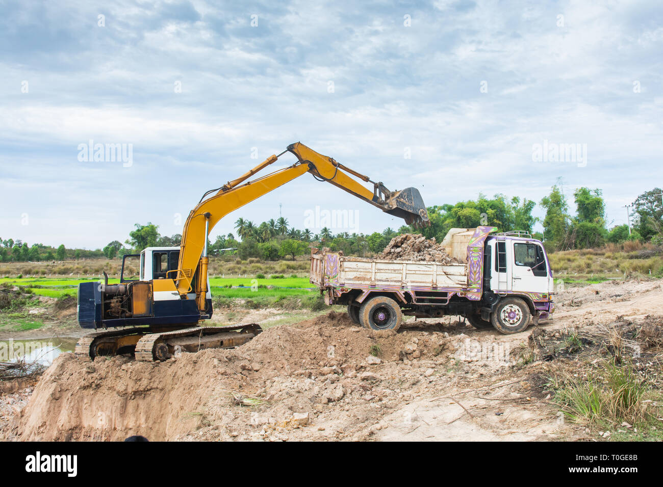 Yellow excavator machine loading soil into a dump truck at construction ...