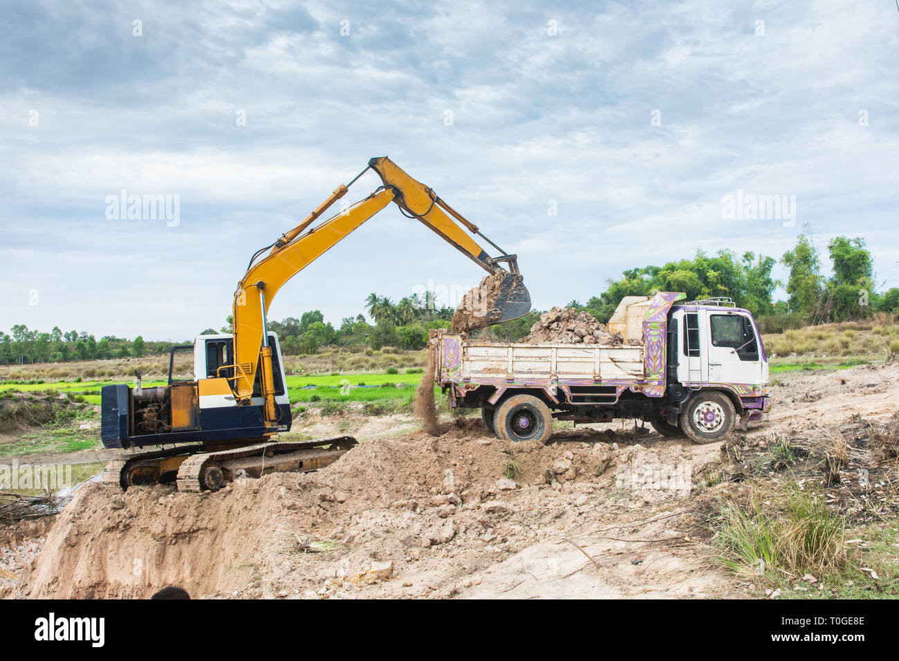 Yellow excavator machine loading soil into a dump truck at construction ...