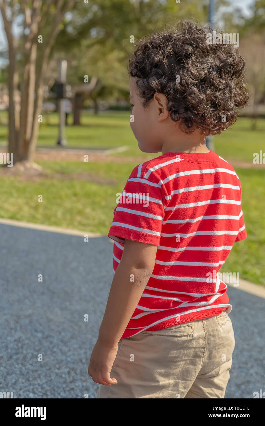 The little boy looks away at the park. He searches for other kids to ...